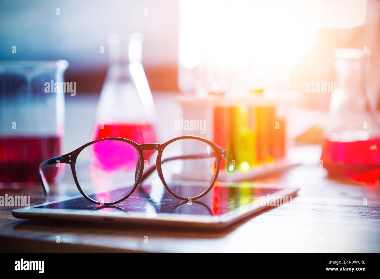 Glasses on tablet screen with blurred science equipments on background ...