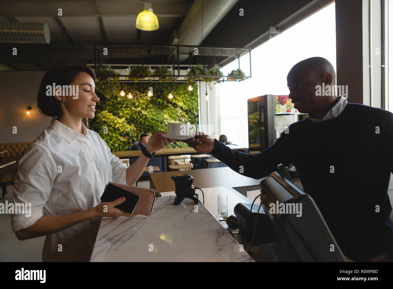 Waiter serving coffee to female executive at counter Stock Photo - Alamy
