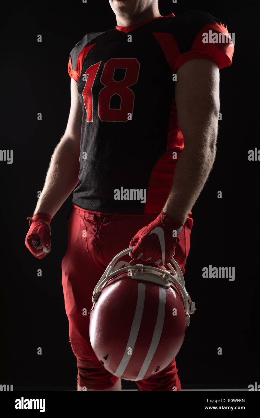 American football player standing with helmet against black background ...