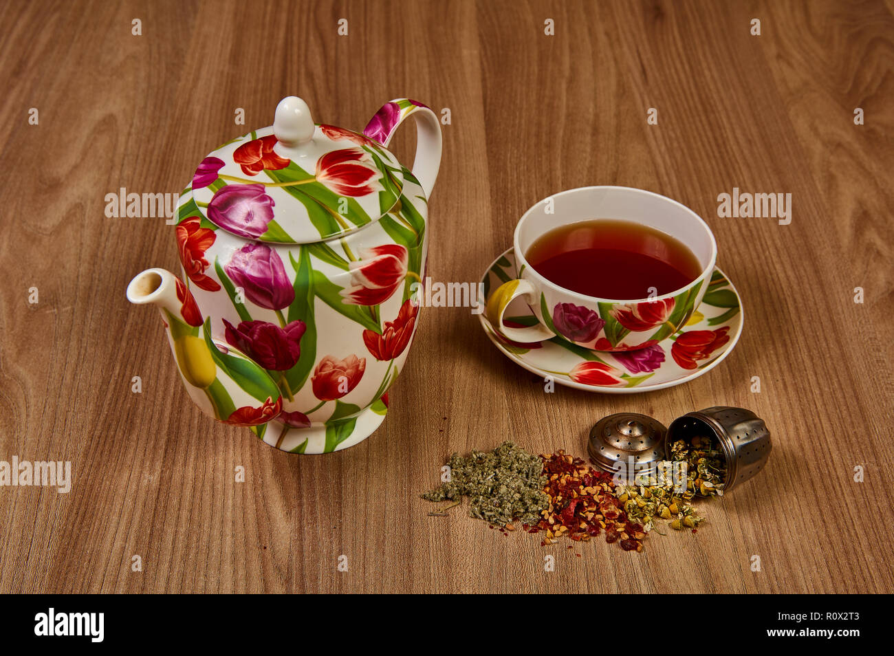 Loose tea spilling from metal egg strainer with cup of tea in ...