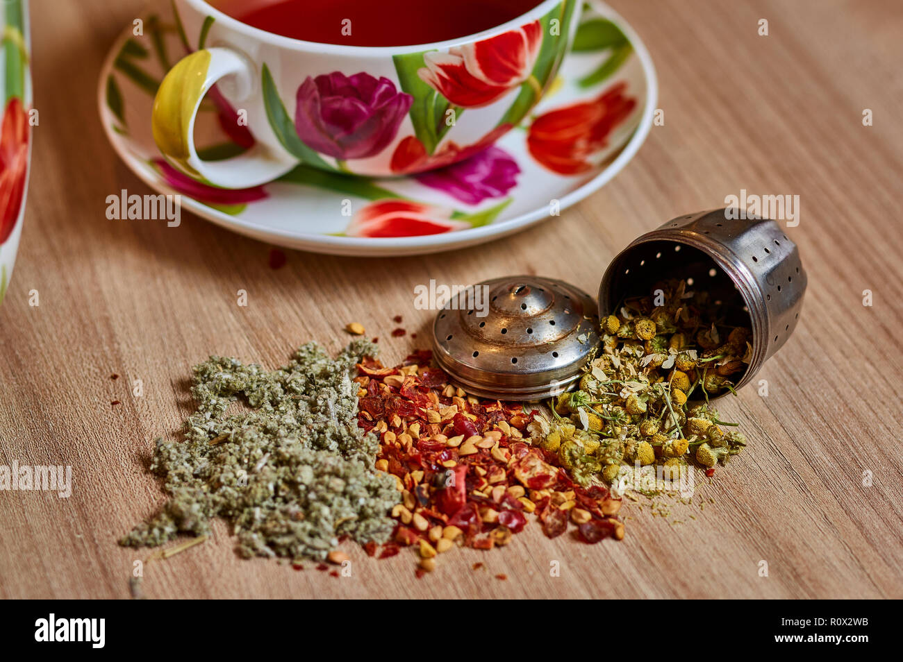 Loose tea spilling from metal egg strainer with cup of tea in ...
