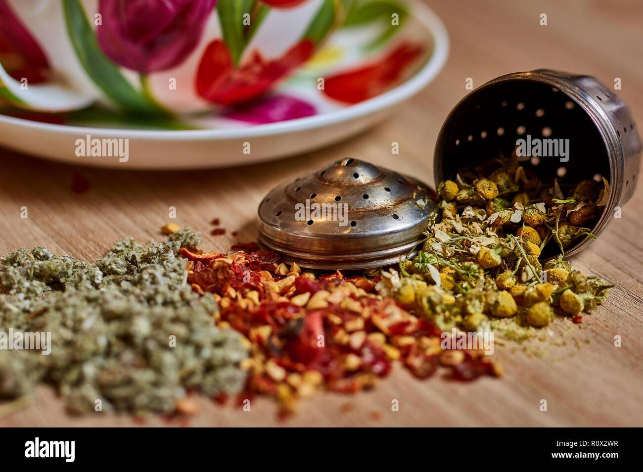 Loose tea spilling from metal egg strainer with cup of tea in ...