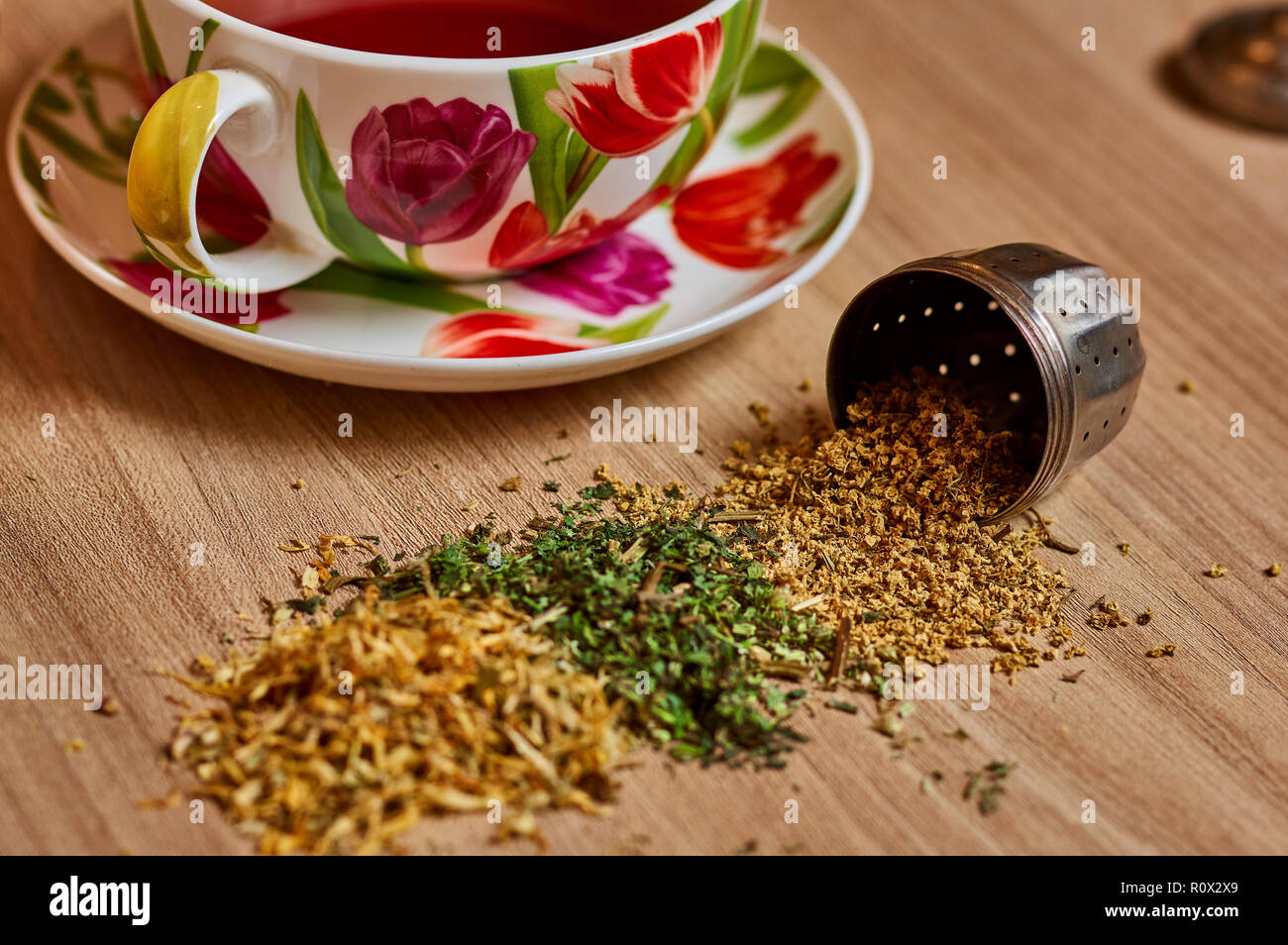 Loose tea spilling from metal egg strainer with cup of tea in ...