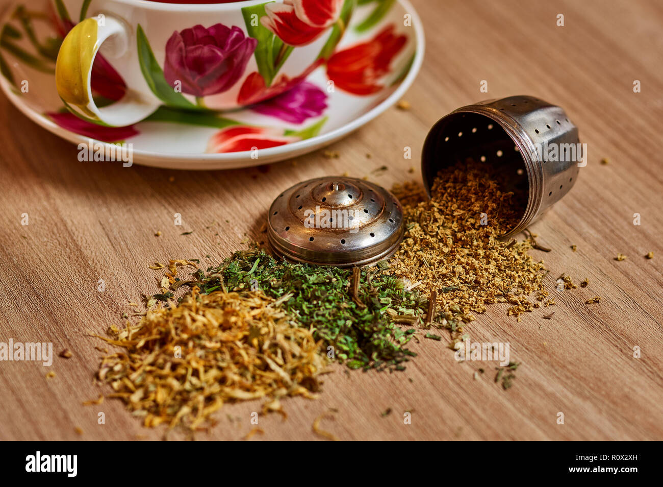 Loose tea spilling from metal egg strainer with cup of tea in ...