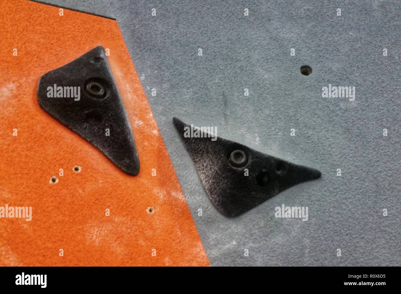 Two black crimper rock climbing holds against an orange and grey wall ...