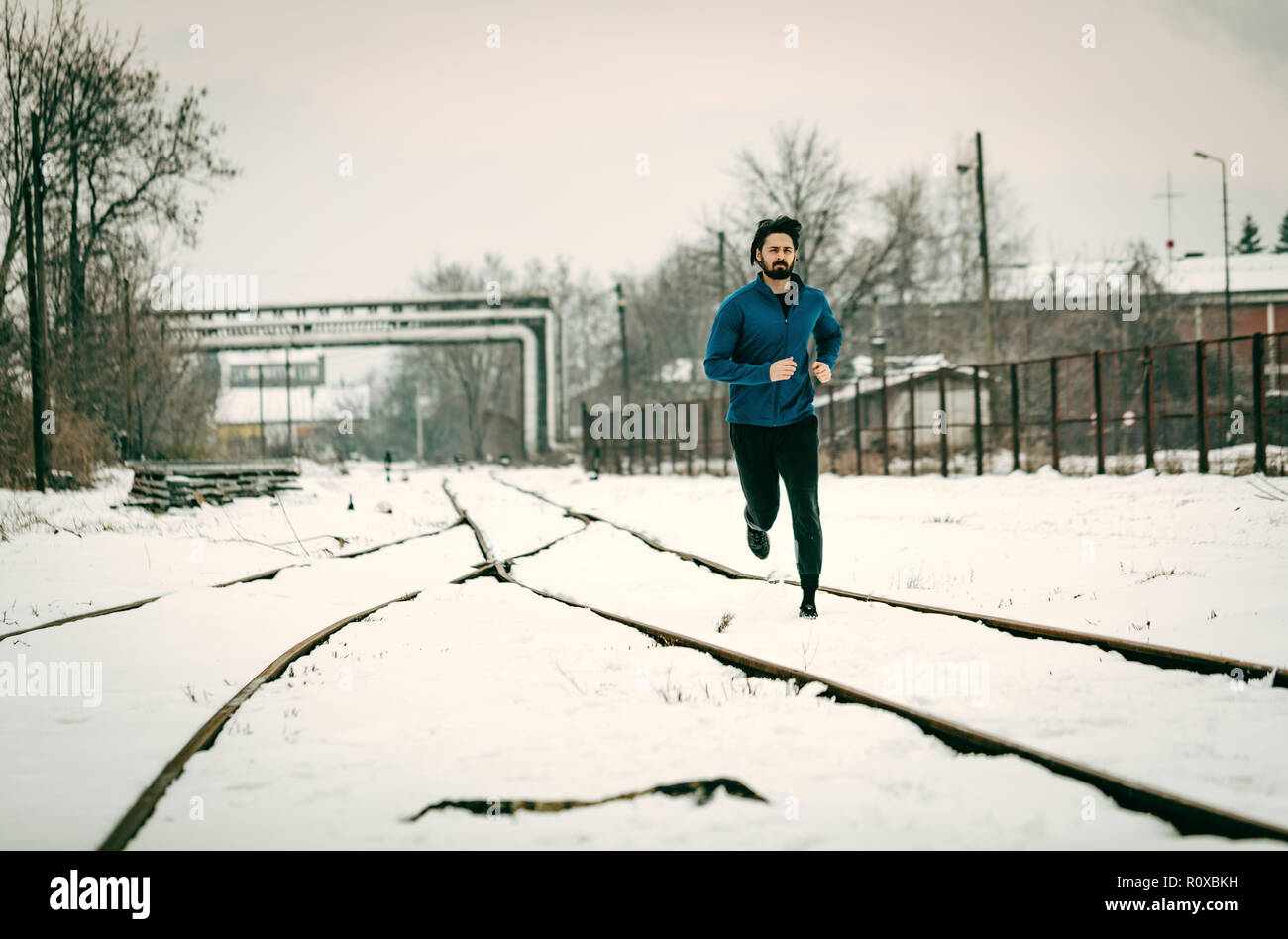 Active young man running and doing exercises across the old railroad ...