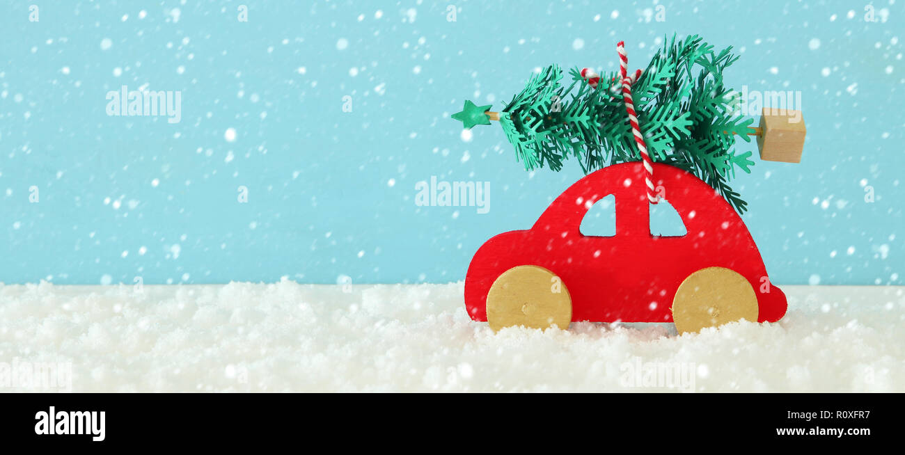 Wooden red car carrying a christmas tree in front of blue background ...