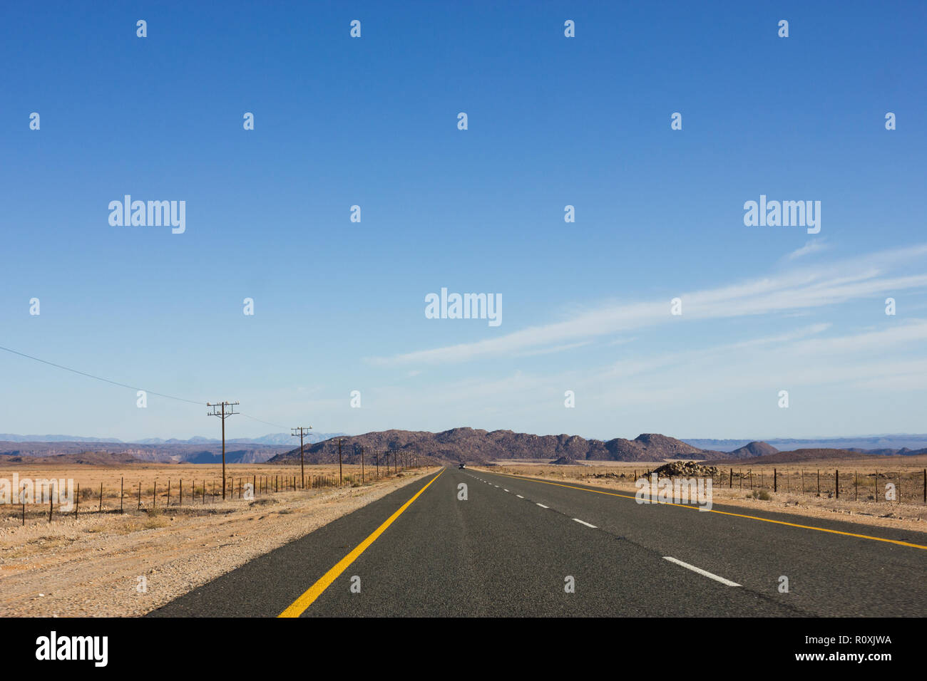 long tarred national road stretches ahead with one car in the distance ...