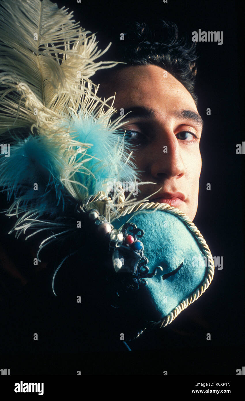 A male mask maker looks at the camera while holding a handmade Venetian ...