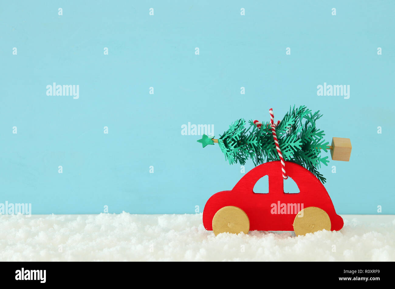 Wooden red car carrying a christmas tree in front of blue background ...