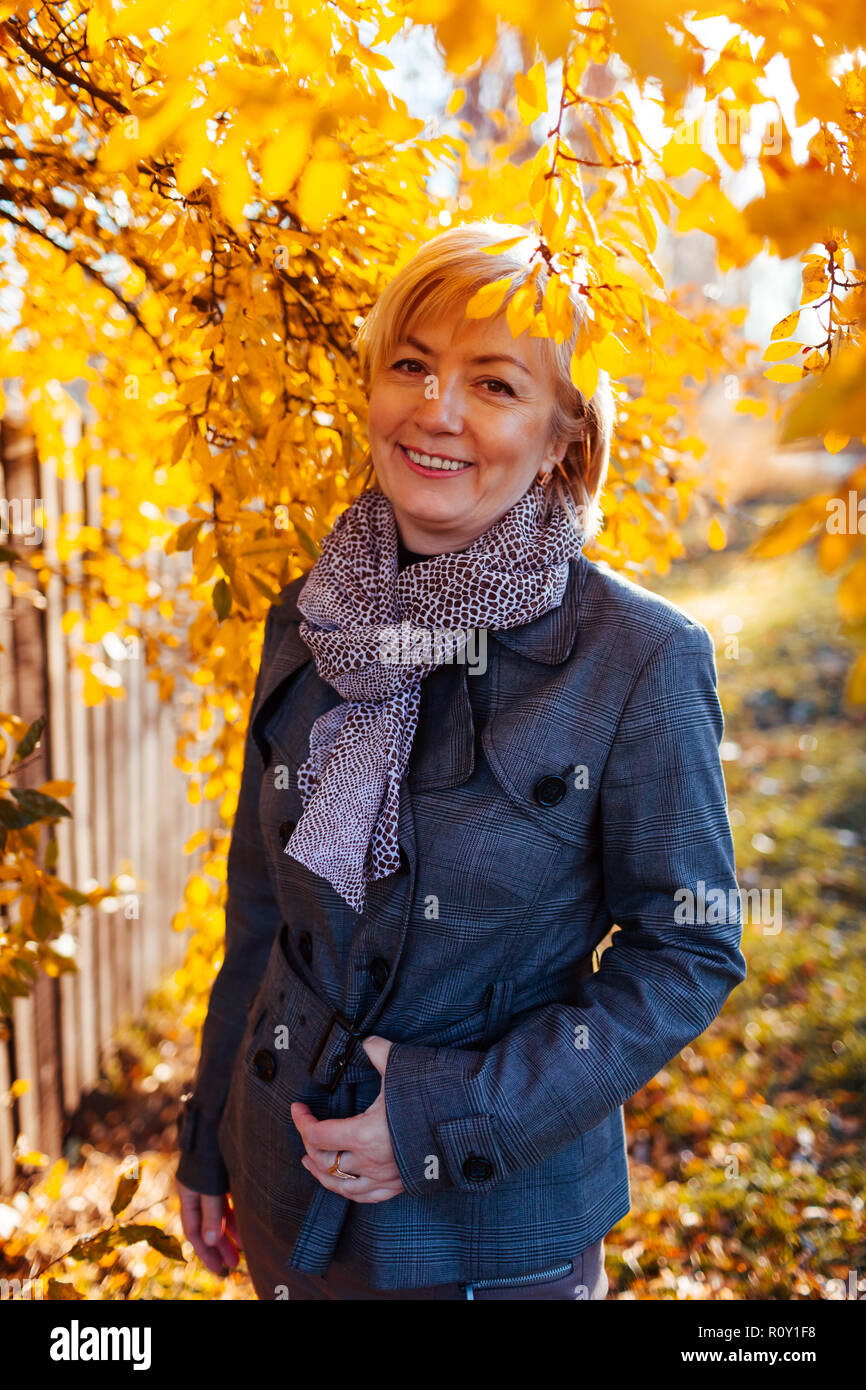 Stylish middle-aged woman posing in autumn park. Senior lady wearing ...