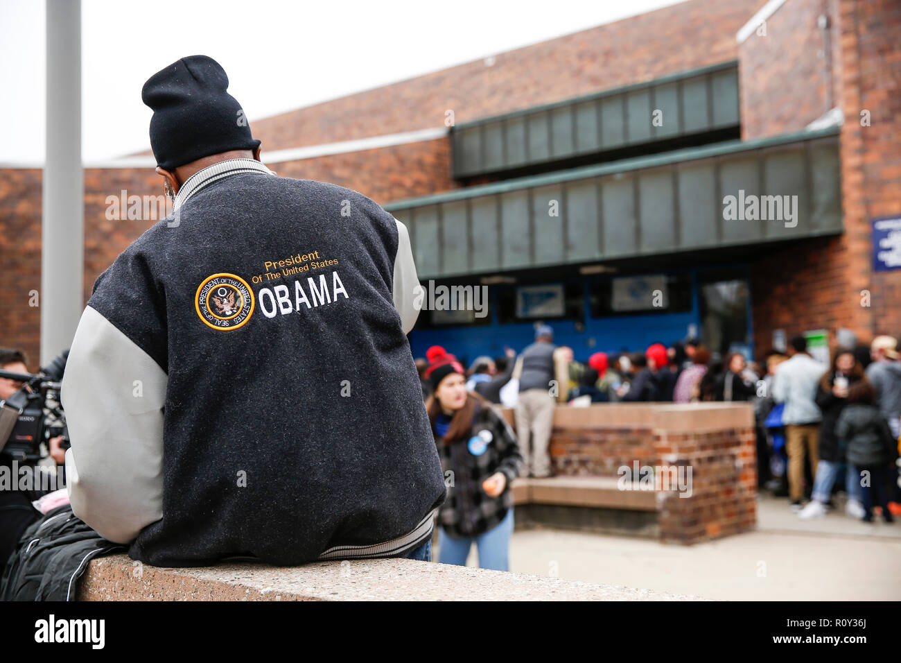 A man sits on a stoop wearing an "Obama" jacket outside of a venue that ...