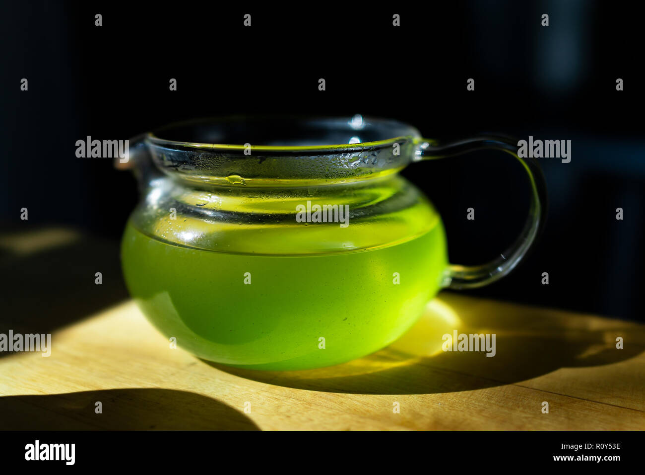 Closeup of glass teapot on wooden table in dark room with sunlight from ...