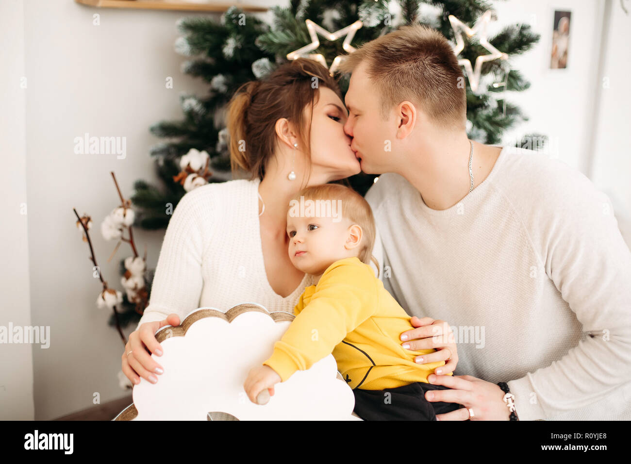 Happy parents in love hugging and kissing sitting on background near ...