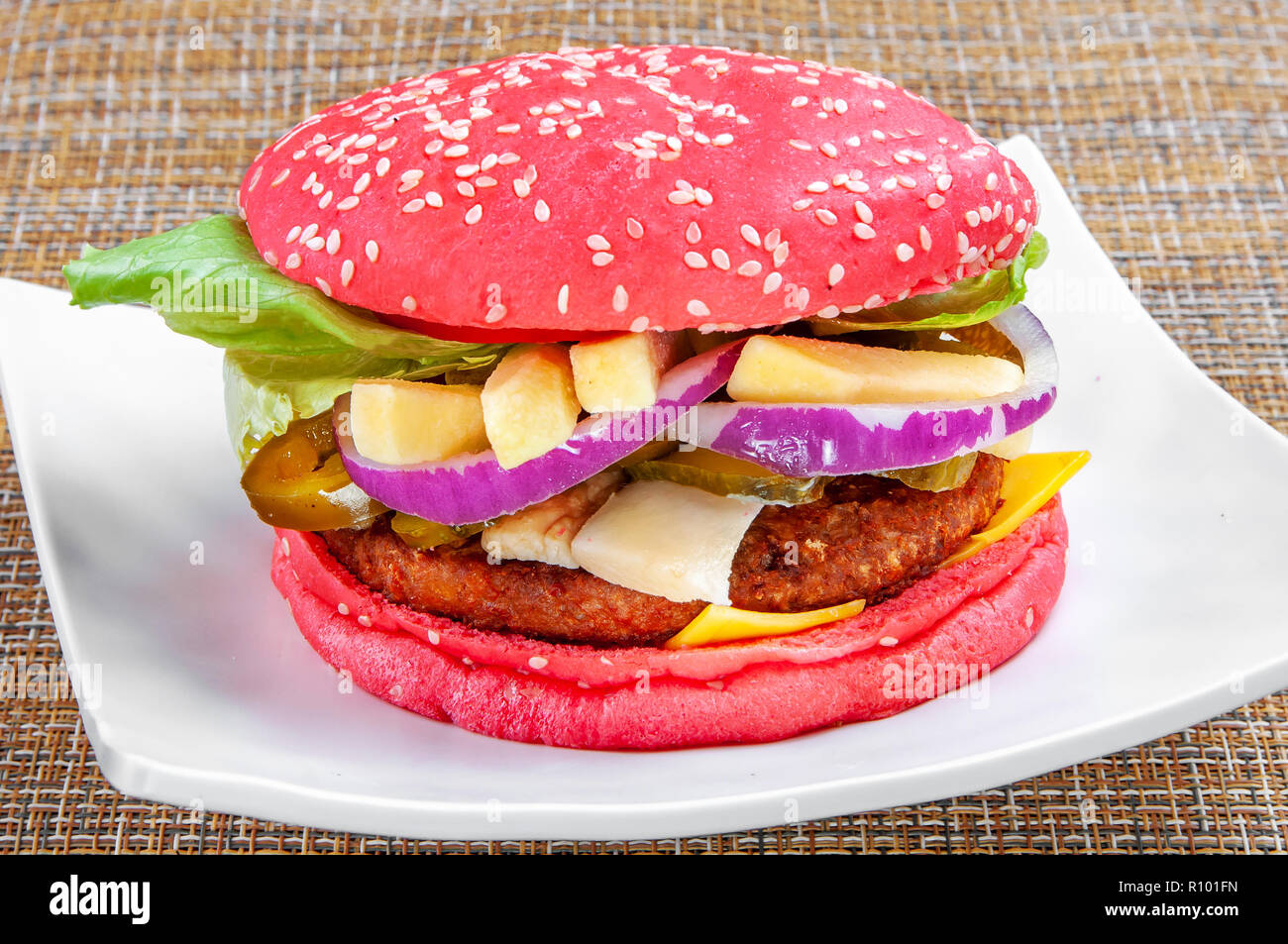 Classic hamburger with red bread and fresh vegetables on a white plate ...