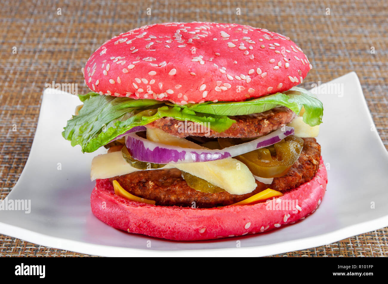 Classic hamburger with red bread and fresh vegetables on a white plate ...