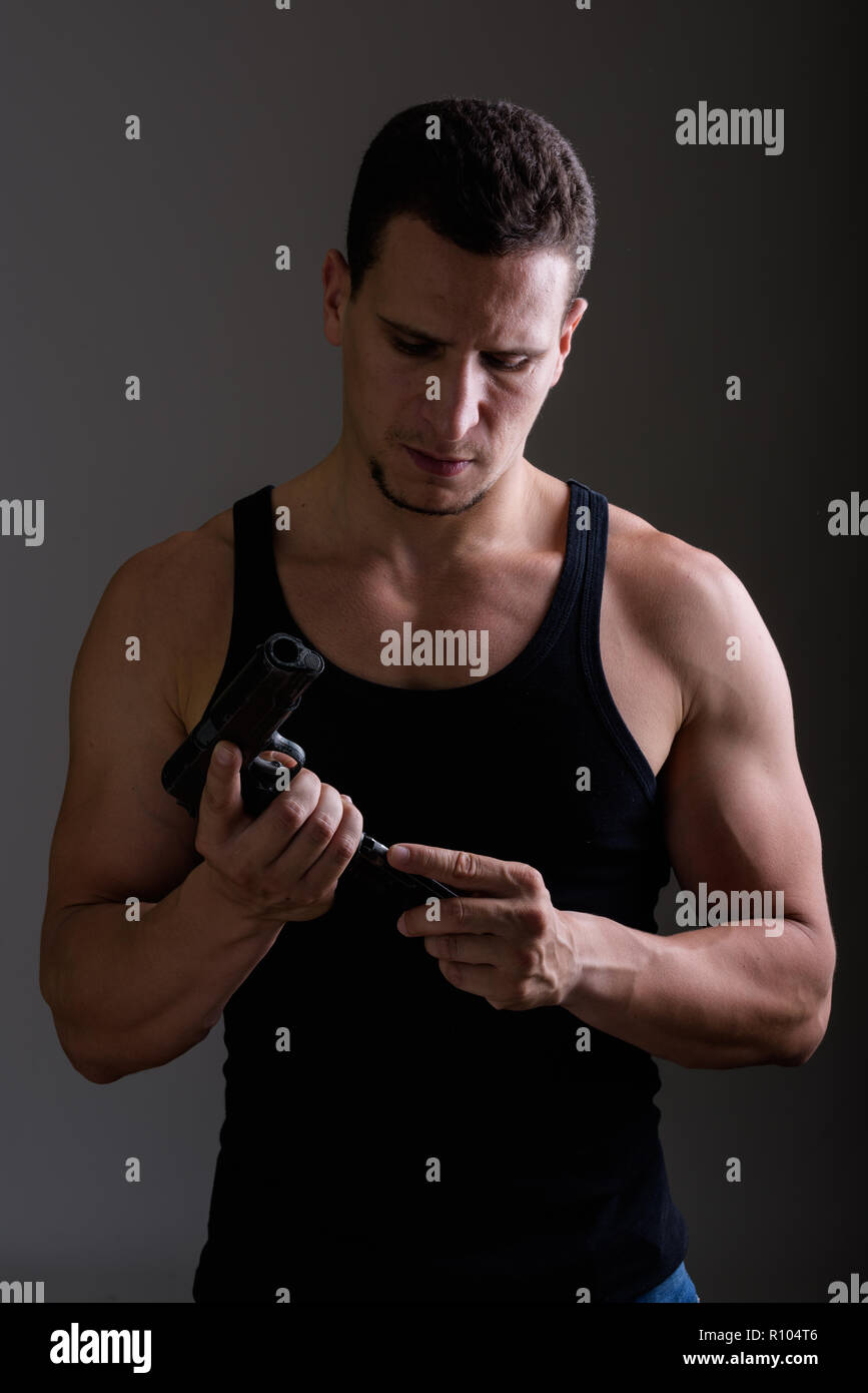 Studio shot of young muscular Persian man reloading gun in dark Stock ...