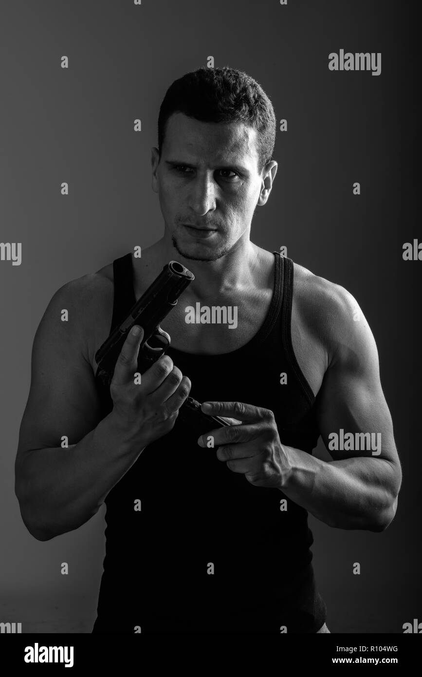 Studio shot of young muscular Persian man reloading gun while th Stock ...
