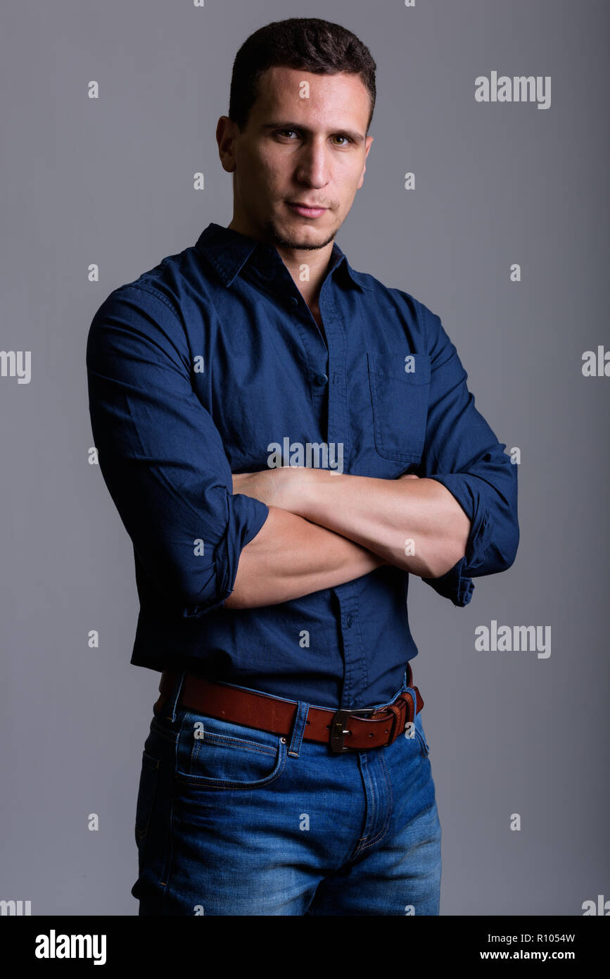 Young muscular Persian man with arms crossed against gray backgr Stock ...
