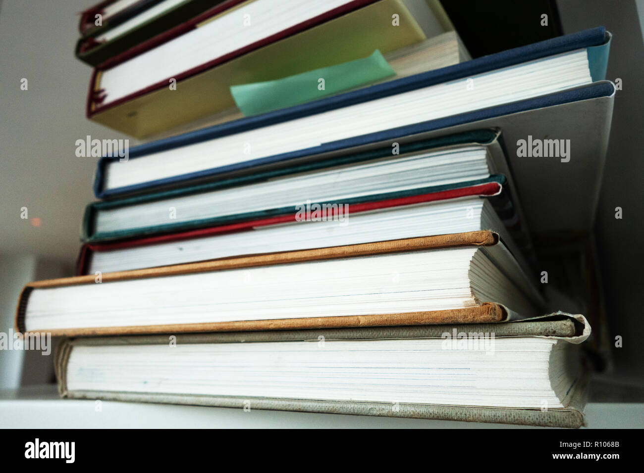 photograph of the sides of a pile of hardbacked books on a white shelf ...