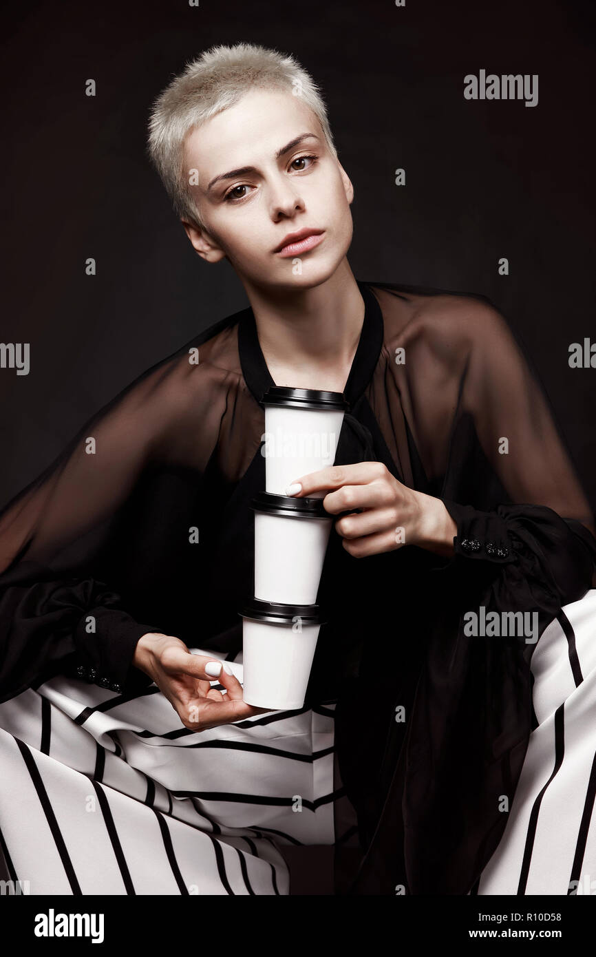 Emotional young girl with short hair and paper coffee cups on black ...