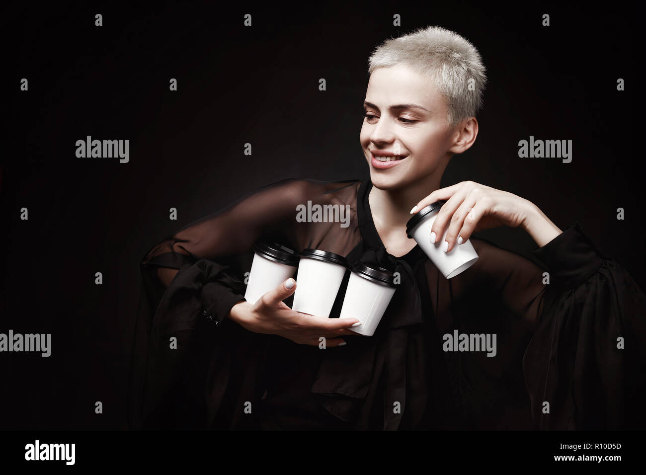 Emotional young girl with short hair and paper coffee cups on black ...