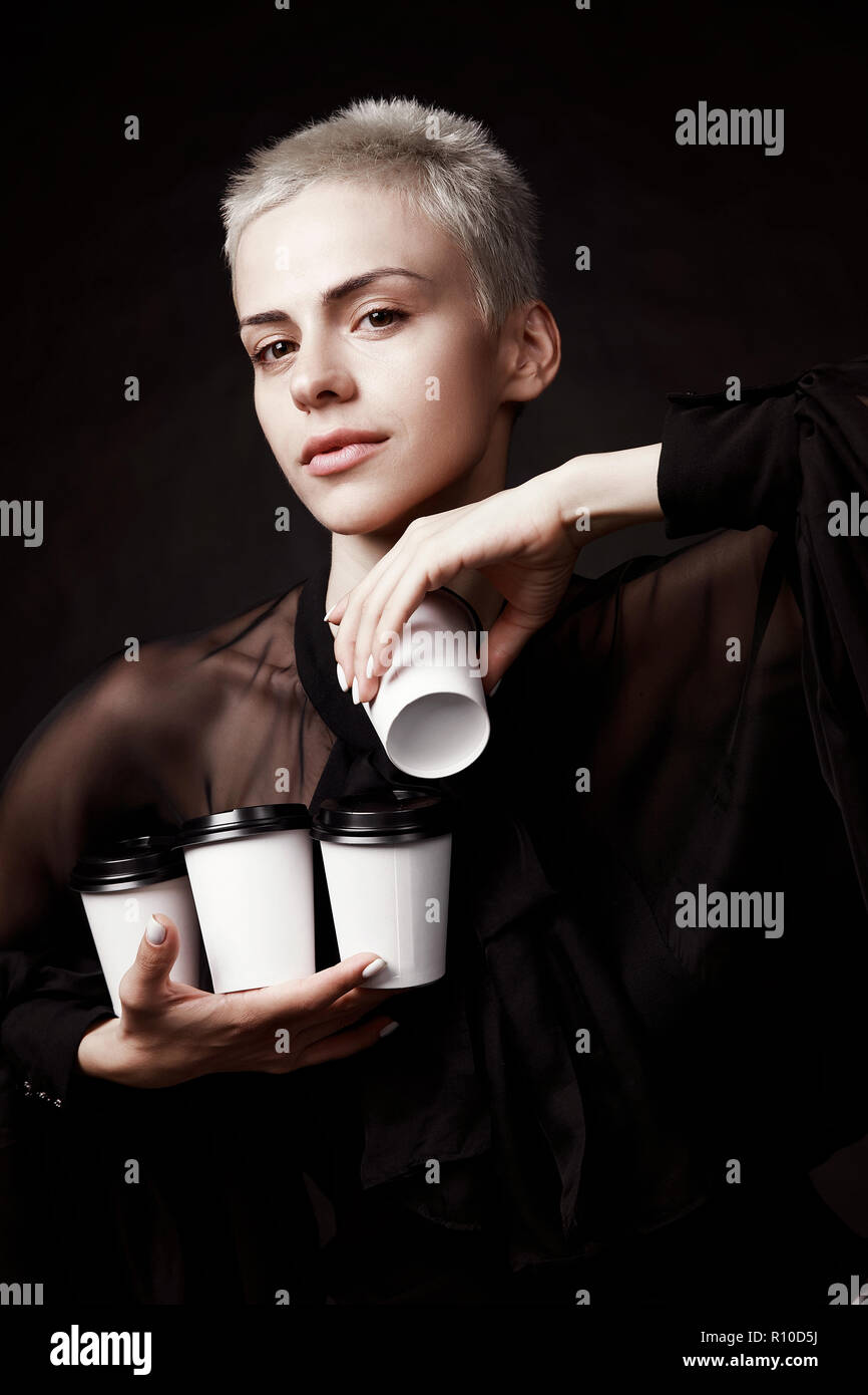 Emotional young girl with short hair and paper coffee cups on black ...