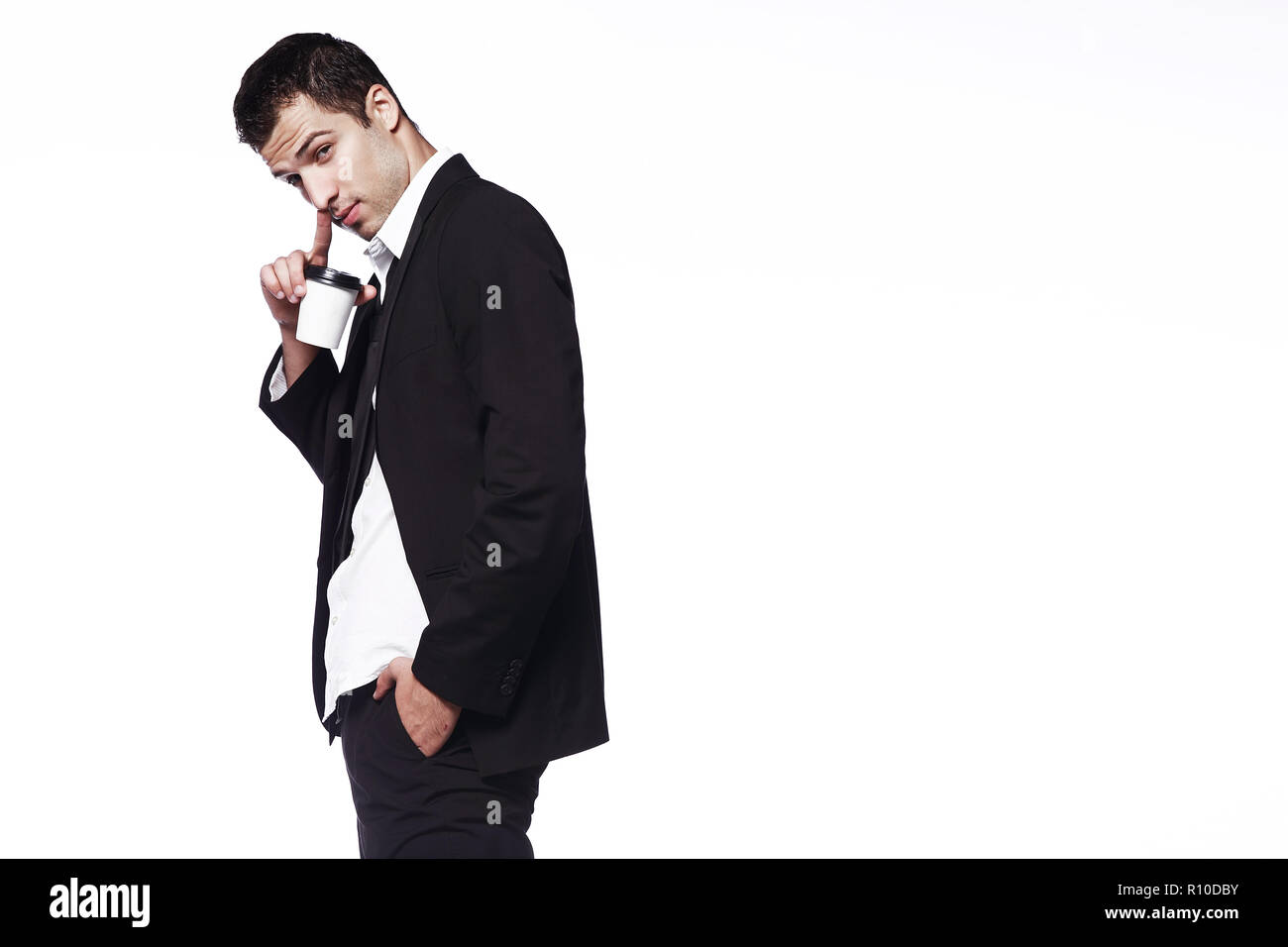 A young guy in a black suit with a coffee Cup on a white background ...