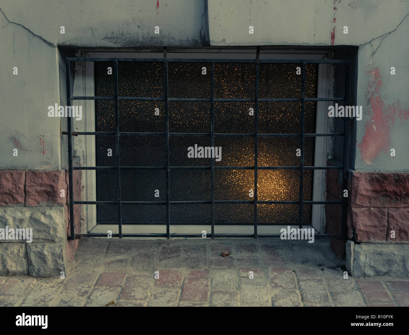 small window of basement with metal grid and dim orange light inside ...