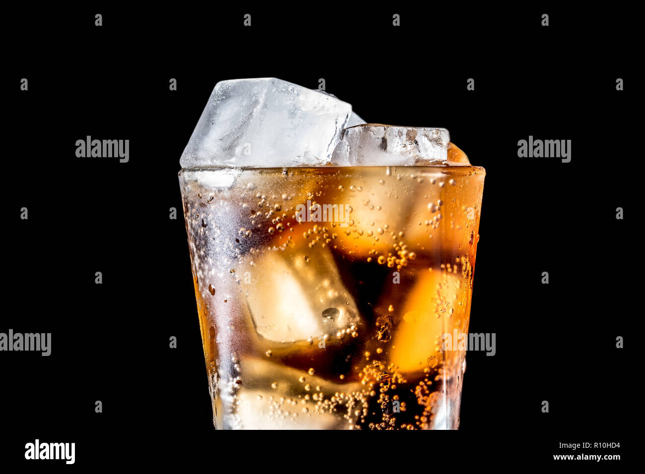 Stream of soda being pouring into a glass with soda and ice cube on black background, closeup ...