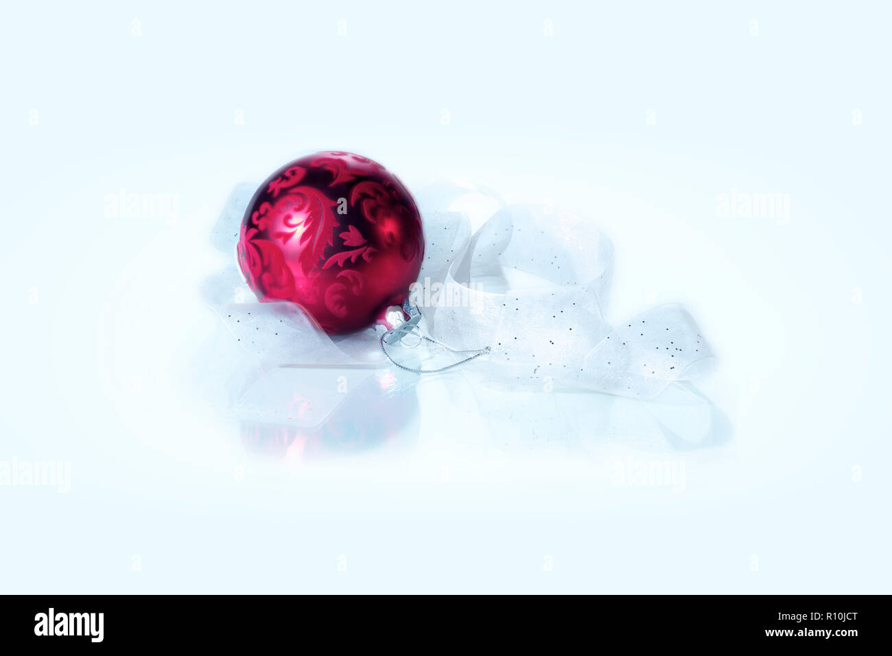 Deep red Christmas bauble with sheer white ribbon in center of image ...