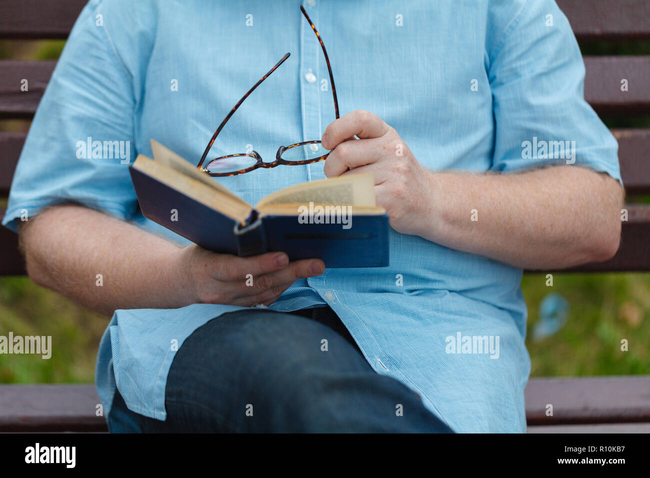 Man sitting on a bench reading a book Stock Photo - Alamy