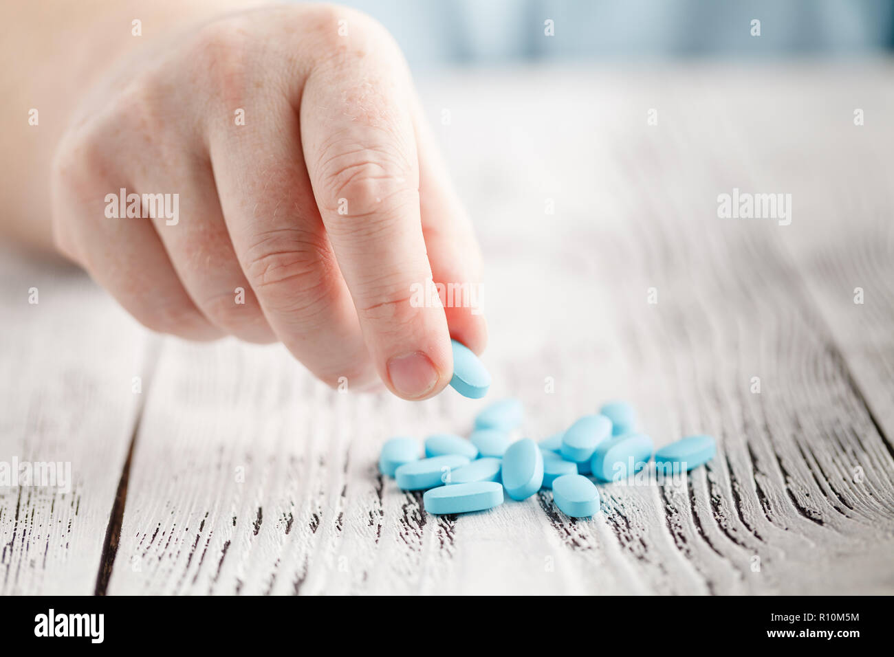 Male hand holding blue pill between fingers Stock Photo - Alamy
