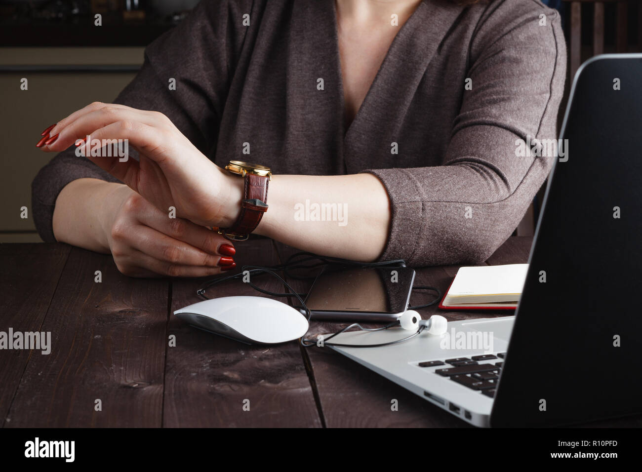 young woman checking time on her watch while working on her laptop at ...