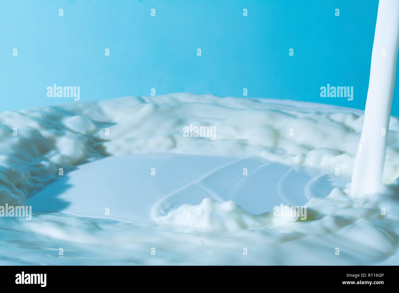 Splash of milk, pouring jet stream of milk on a light blue background ...