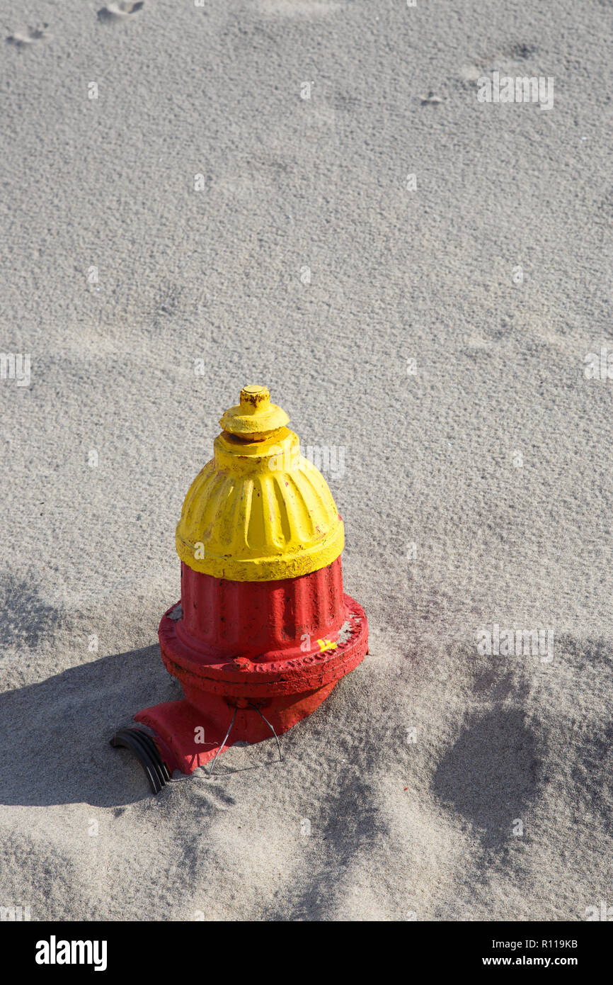 A colorful red fire hydrant with a yellow top nearly covered with sand ...