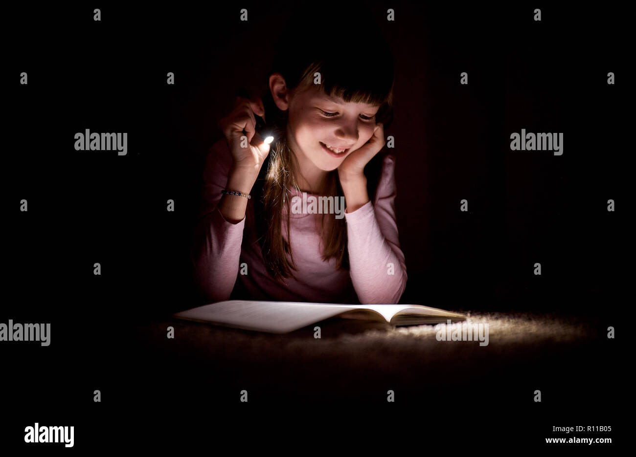 little girl is reading a book with a flashlight in a dark room at night ...