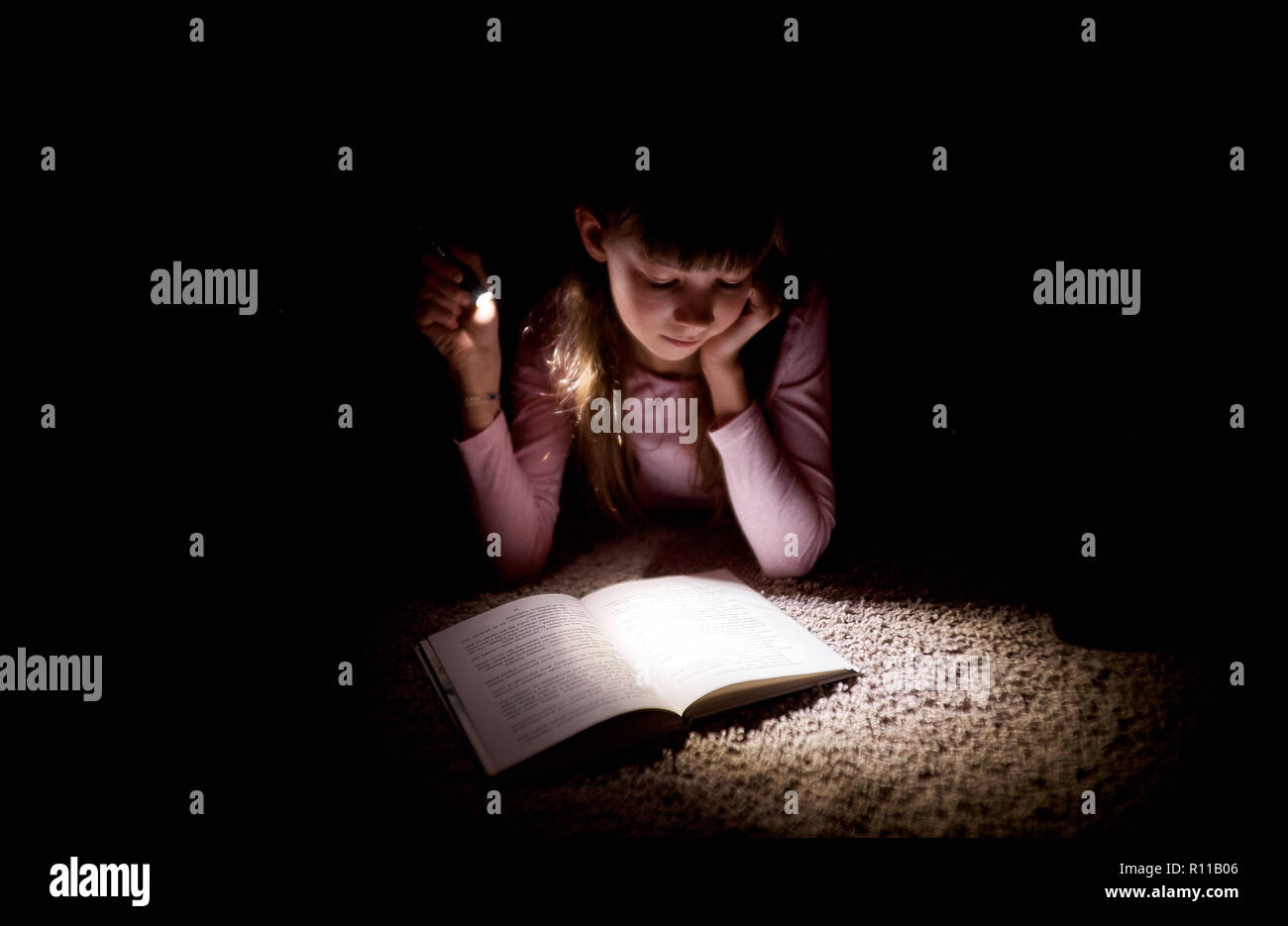 little girl is reading a book with a flashlight in a dark room at night ...