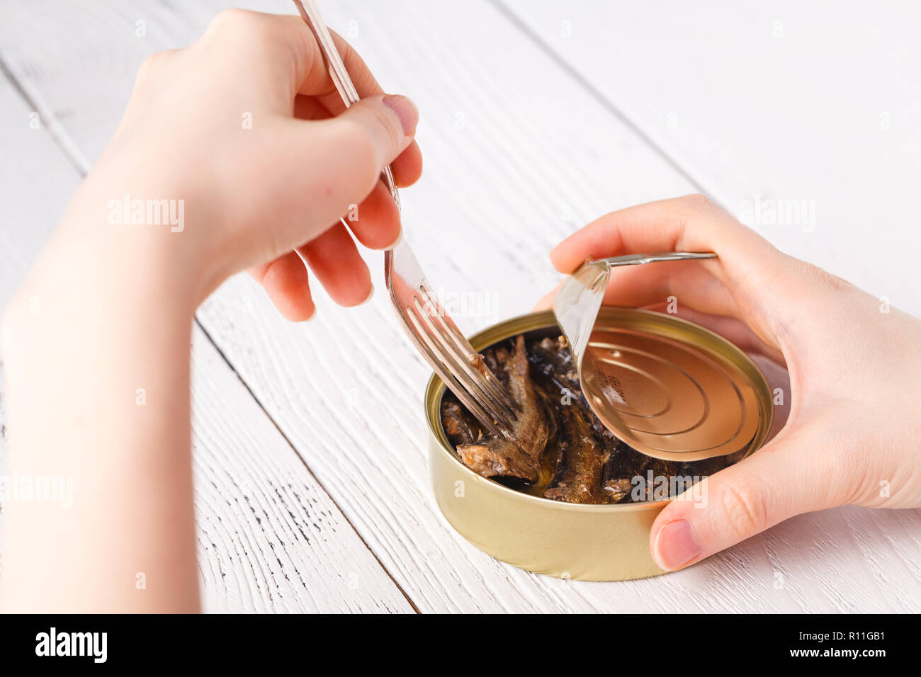 Open fish can with hands and fork on table Stock Photo - Alamy