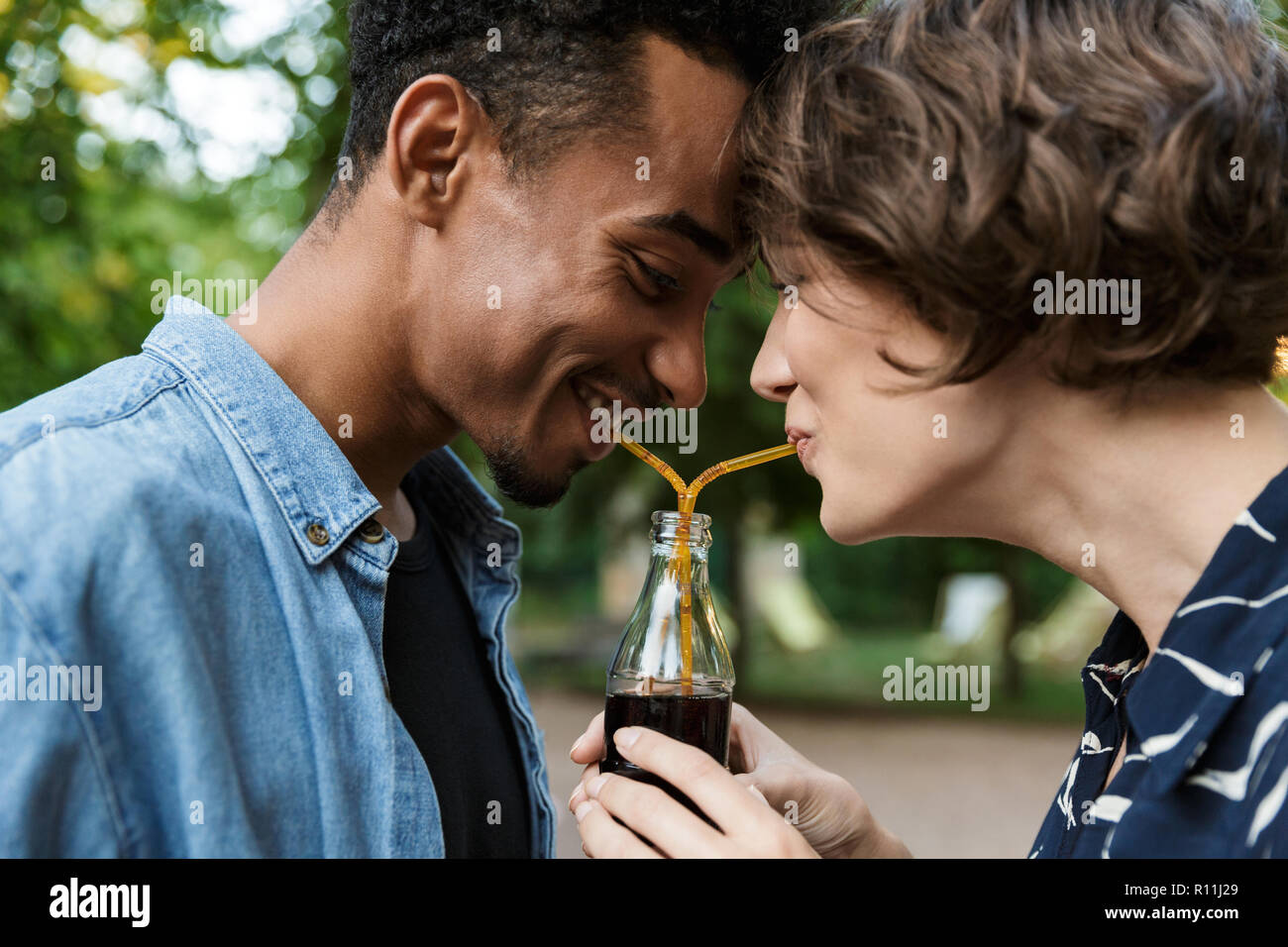 Image of happy young loving couple outdoors in park having fun drinking ...