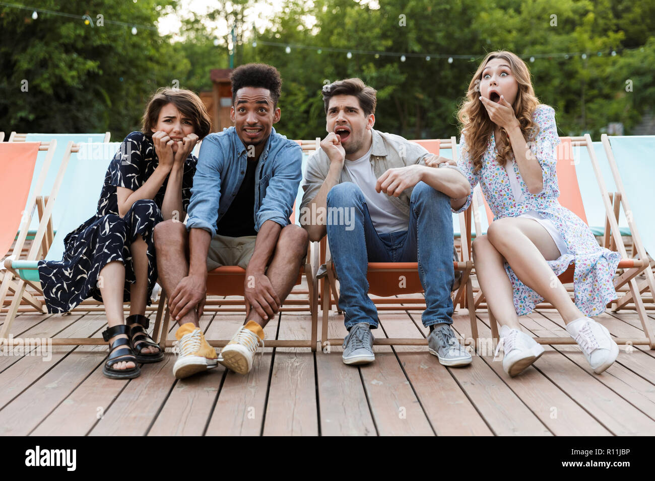 Image of shocked scared young group of friends sitting outdoors looking ...