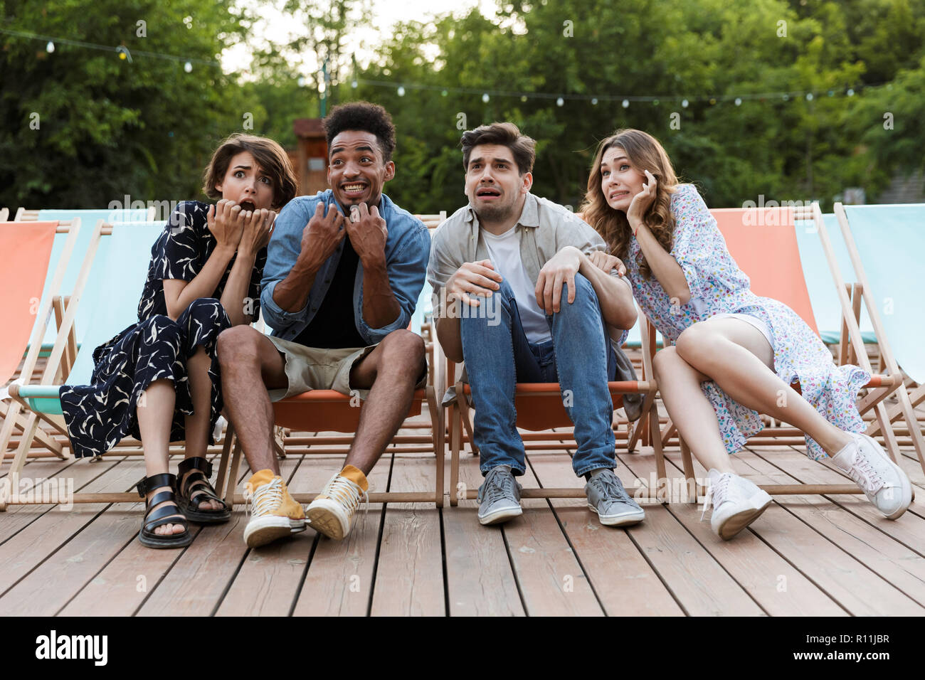 Image of shocked scared young group of friends sitting outdoors looking ...