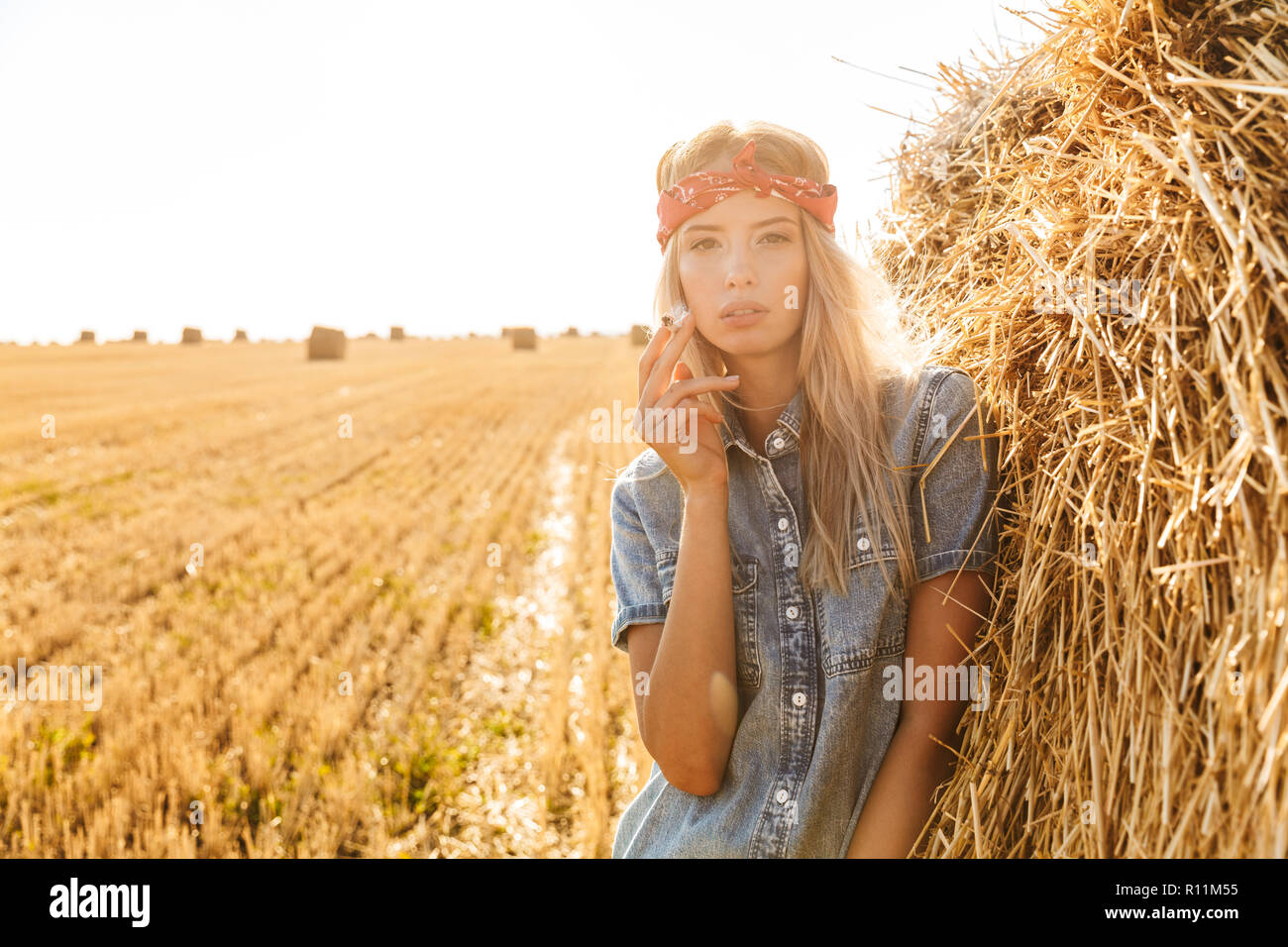 Image of stylish woman 20s standing near big haystack in golden field ...