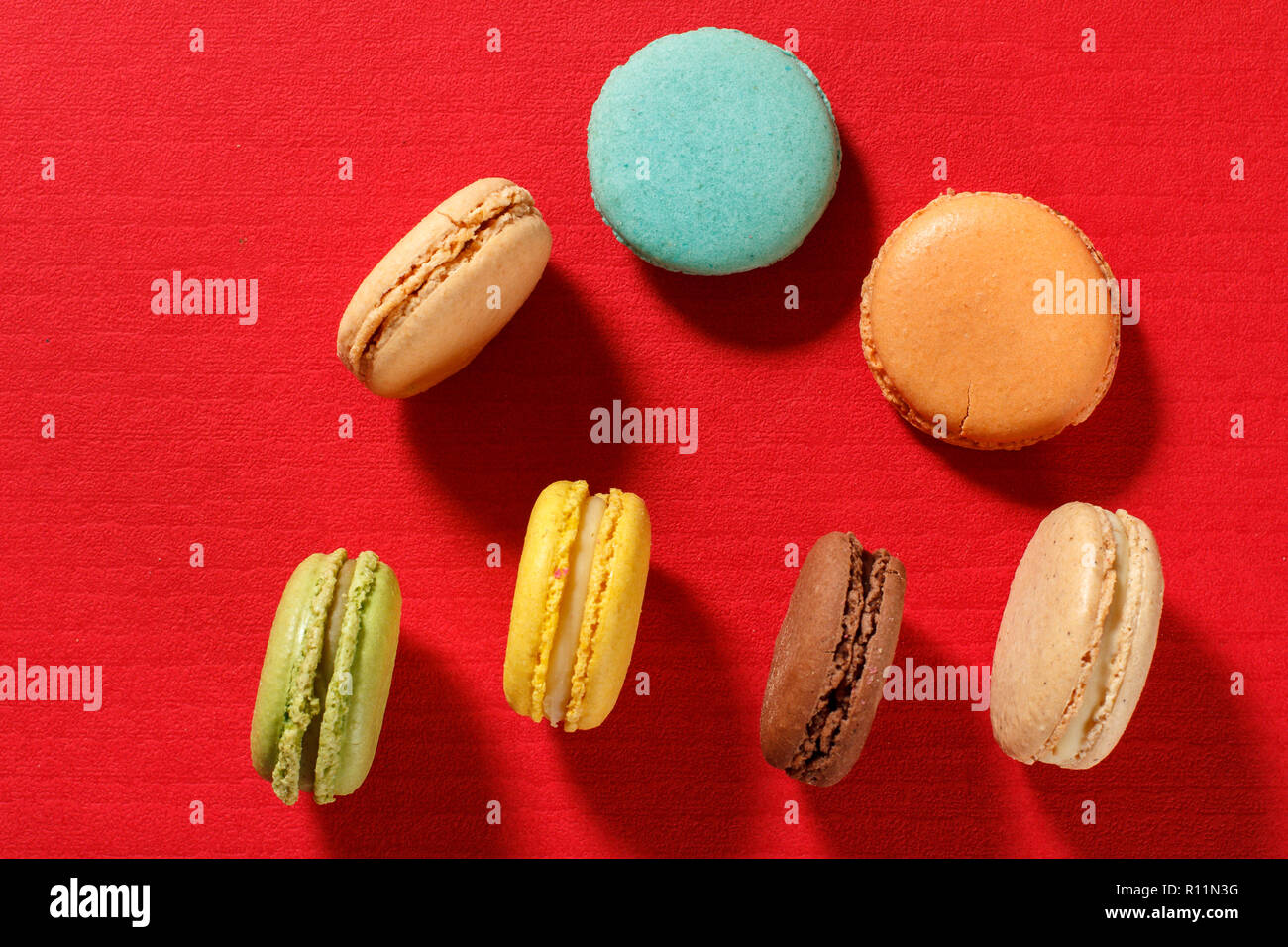 Sweet macarons cakes of different color on red textured surface. Top ...