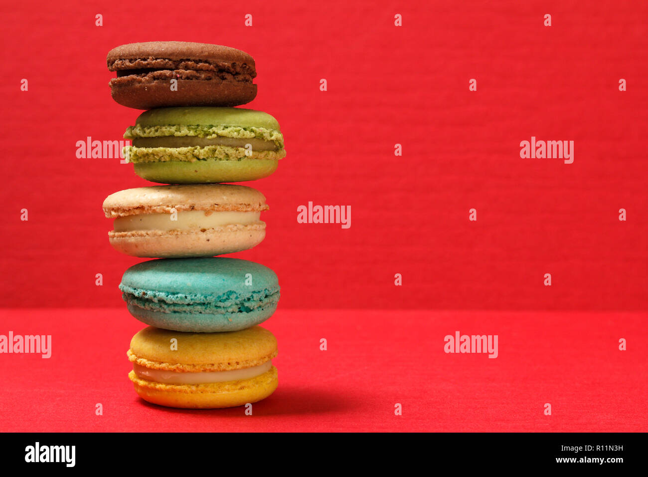 Stacked sweet macarons cakes of different color on red textured surface ...