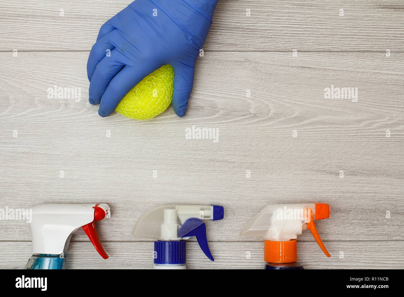 Hand in rubber glove holding synthetic sponge for cleaning with bottles ...
