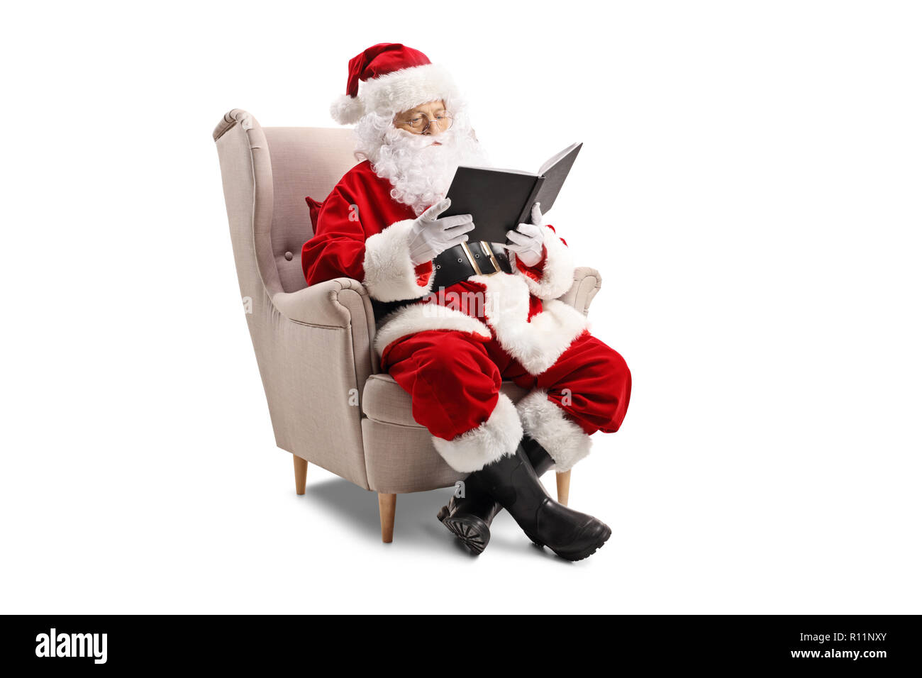 Santa Claus sitting in an armchair and reading a book isolated on white ...