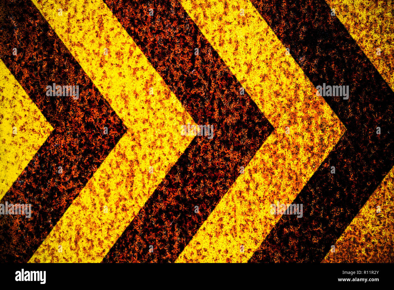 Warning sign yellow and black stripes as arrows painted over rusty ...