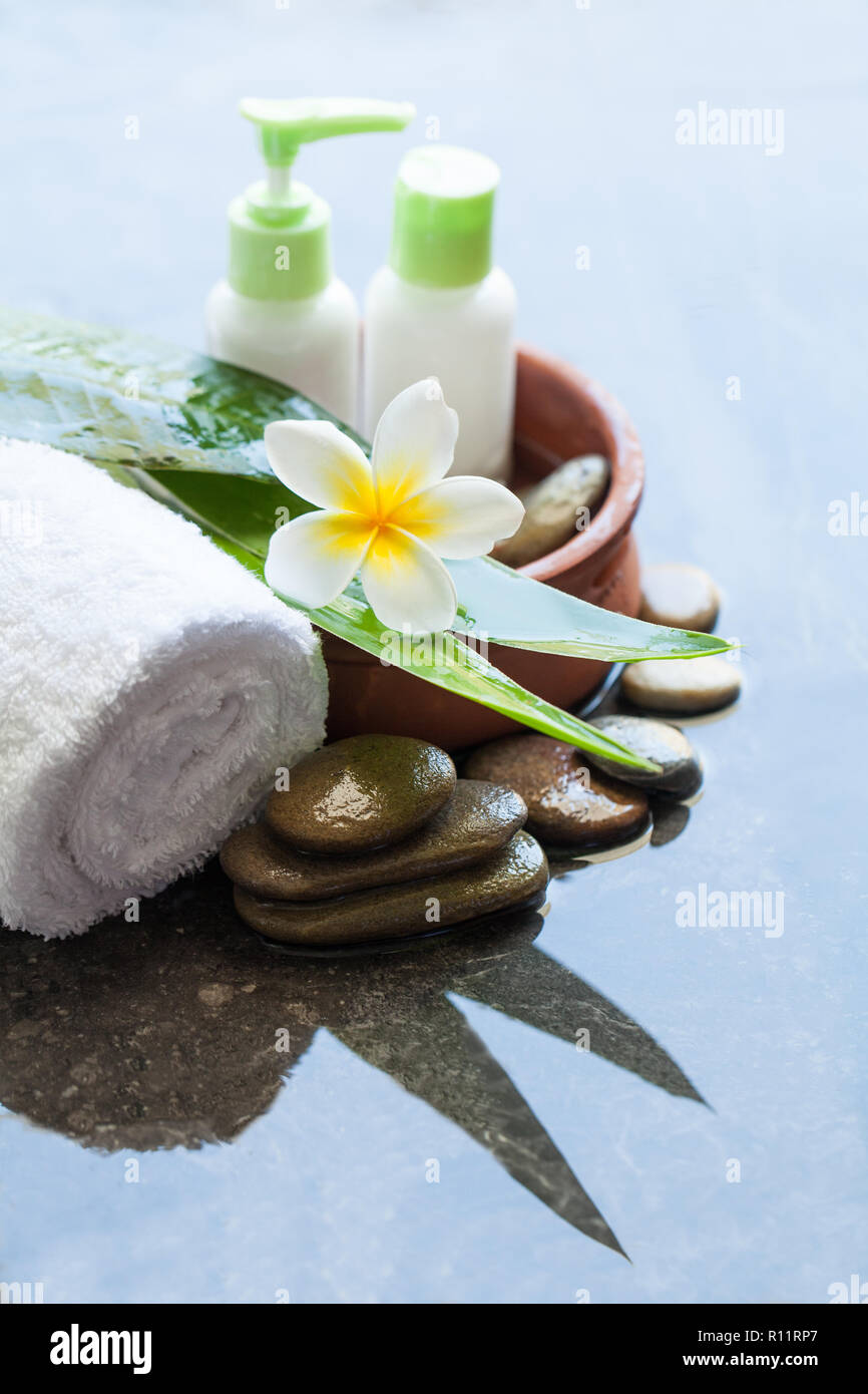 Spa bottles in bowl of water, towel, flower and stones. Body care and ...