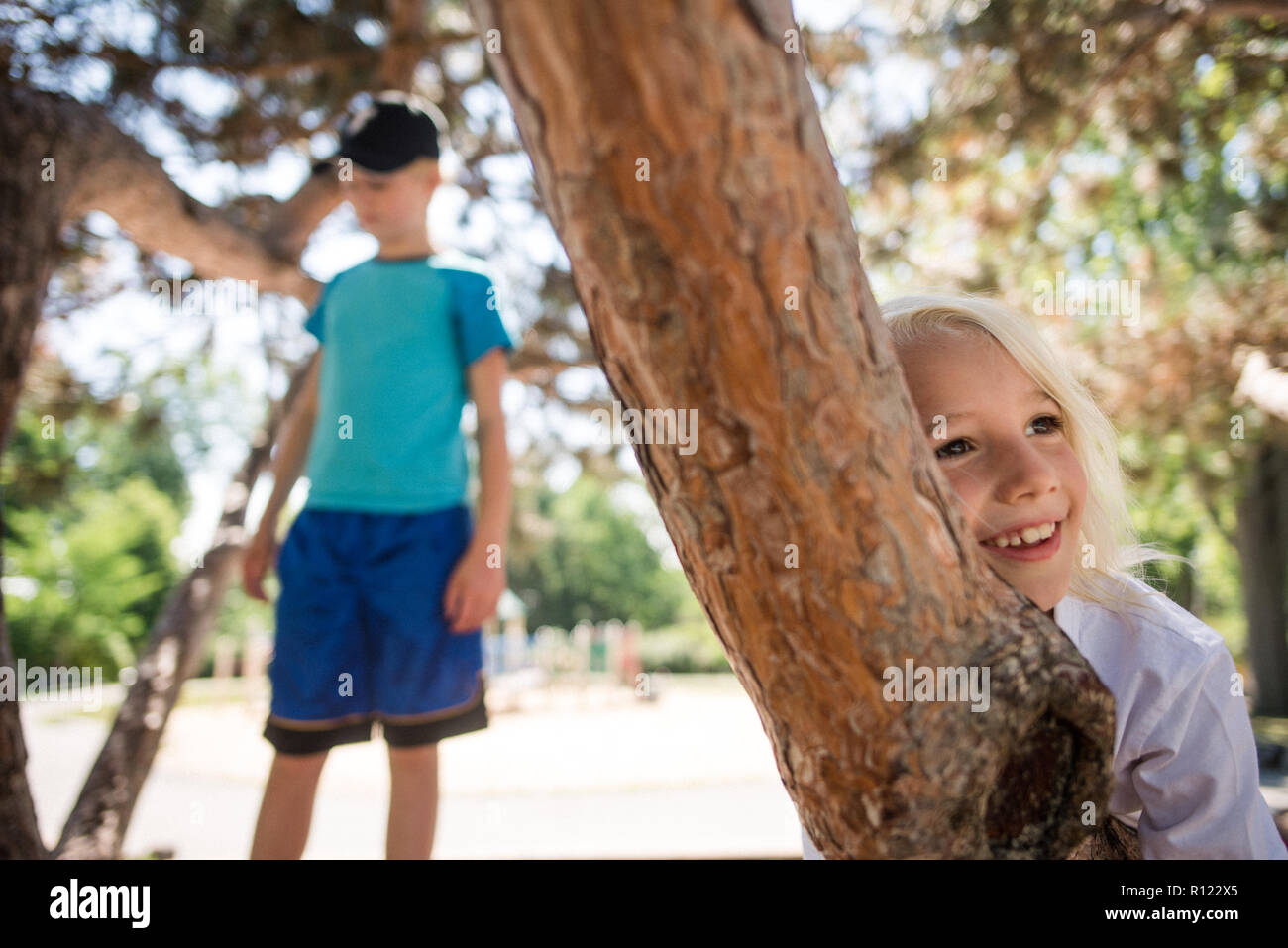 Happy boy leaning against tree branch, sister in background Stock Photo ...